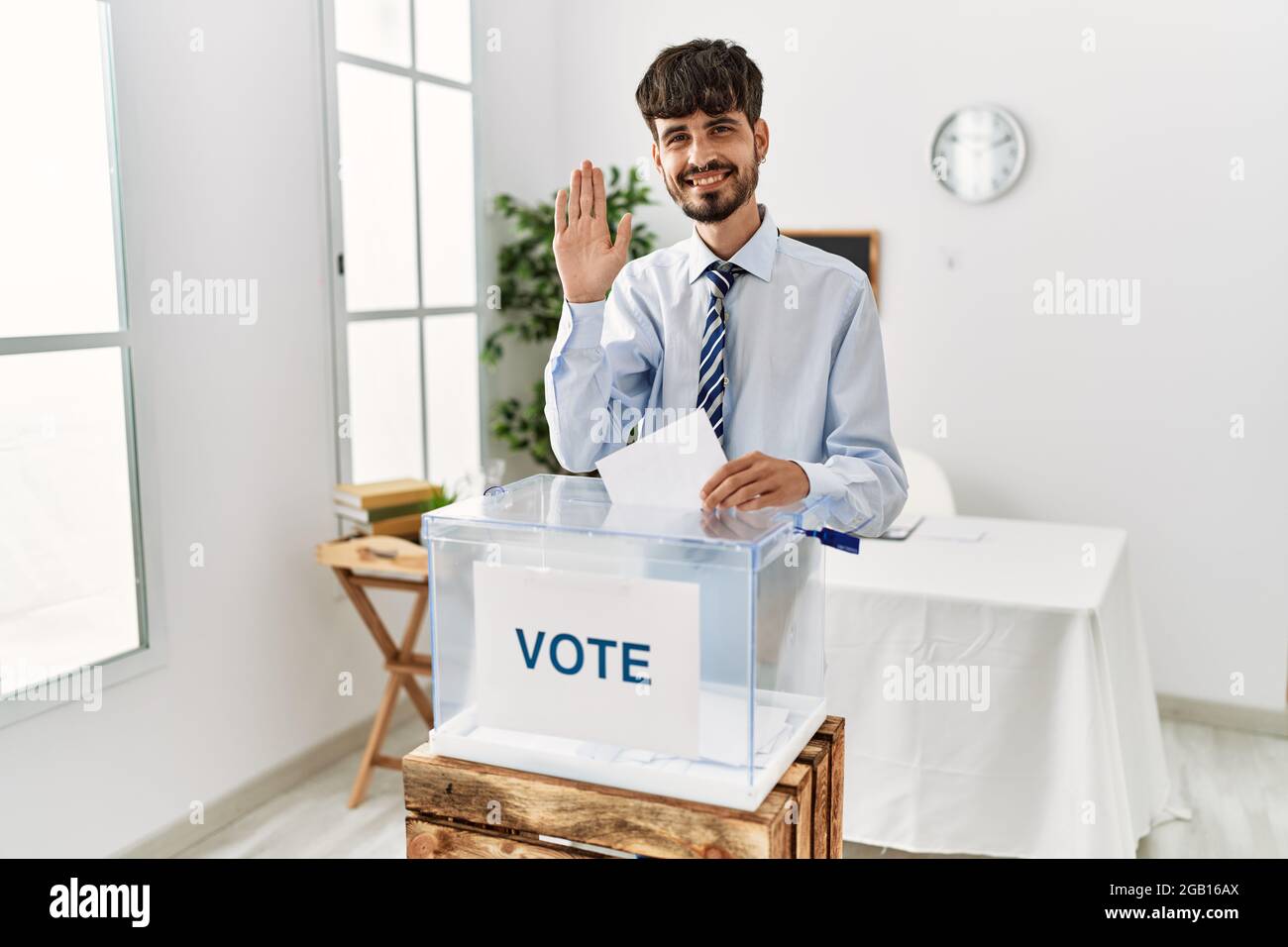 Hispanic man with beard voting putting envelop in ballot box waiving ...