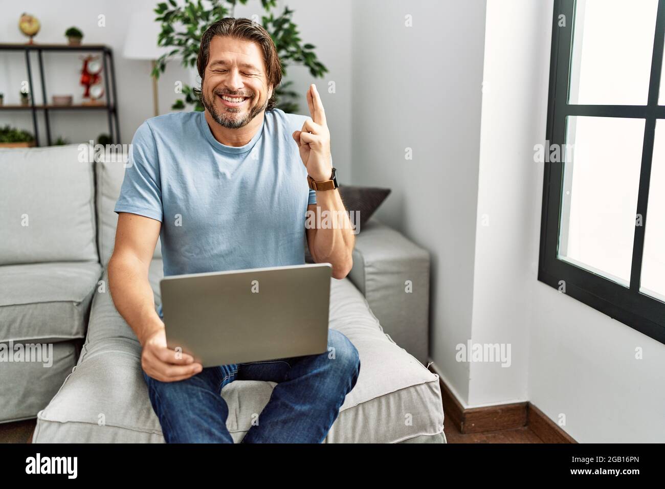 Handsome middle age man using computer laptop on the sofa gesturing ...