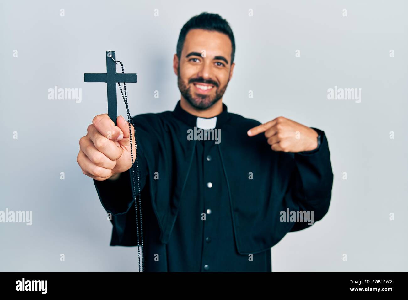 Handsome hispanic priest man with beard holding catholic cross pointing ...
