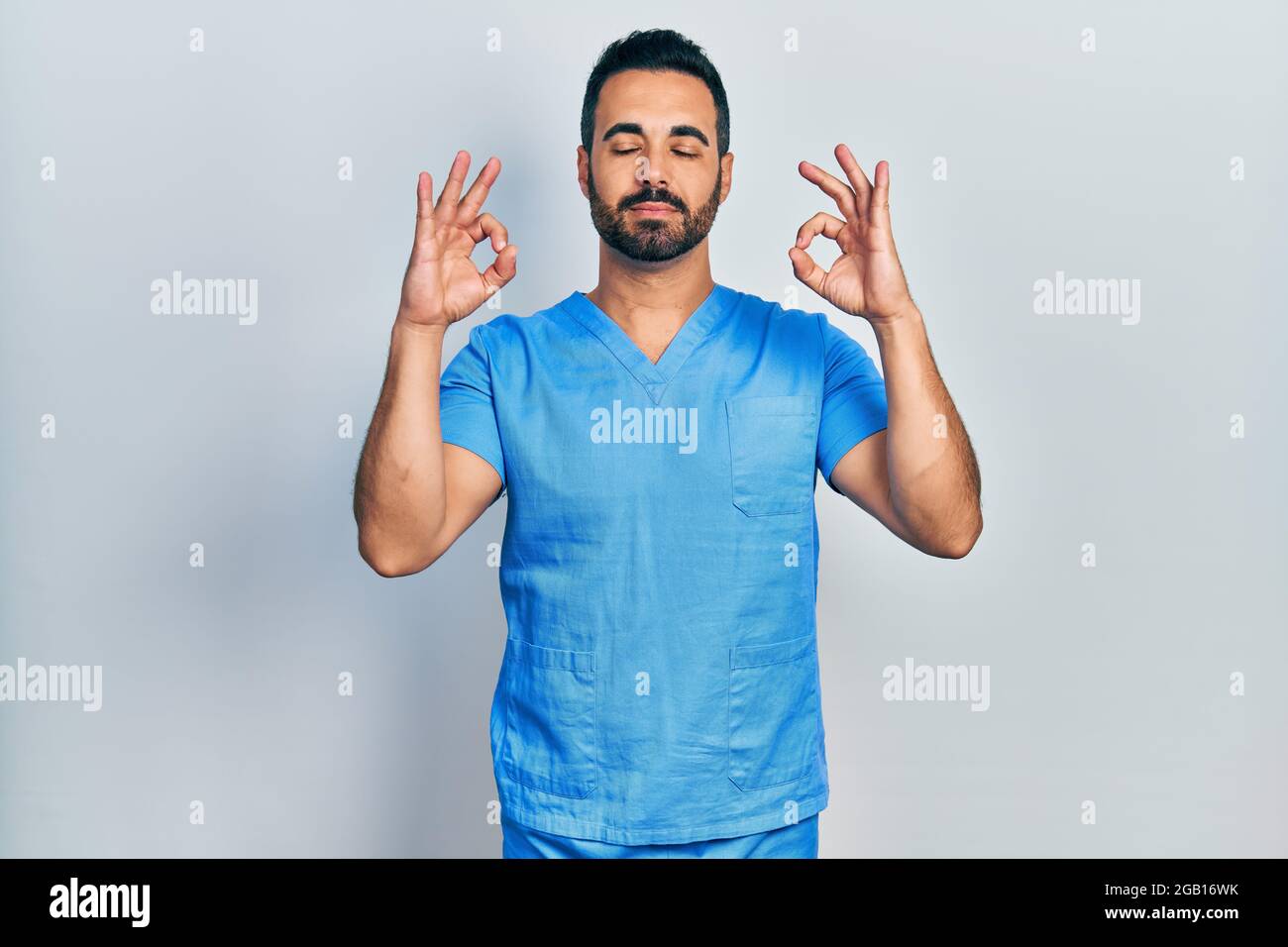 Handsome hispanic man with beard wearing blue male nurse uniform relax ...