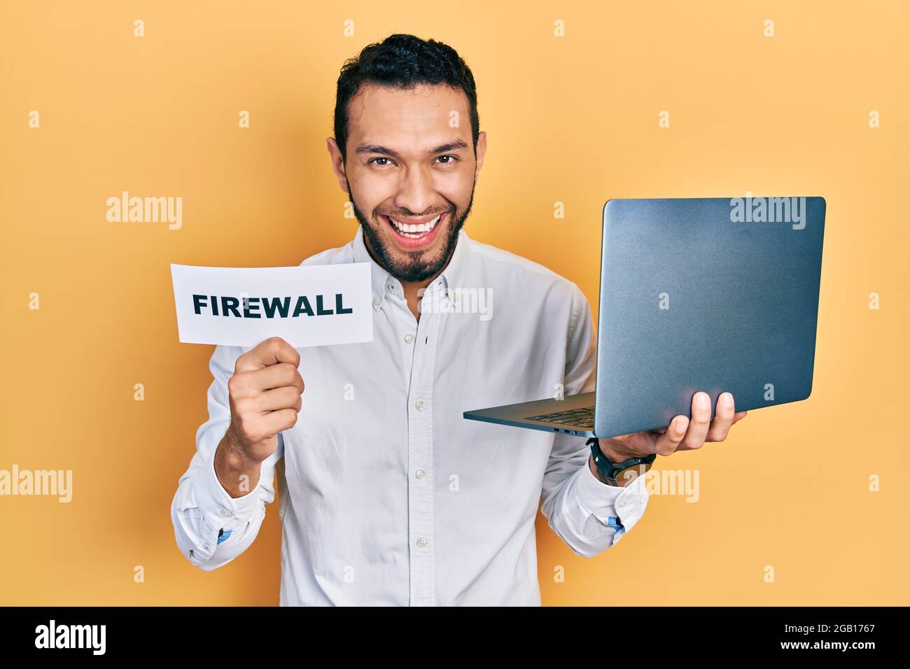 Hispanic man with beard holding computer laptop and firewall banner ...