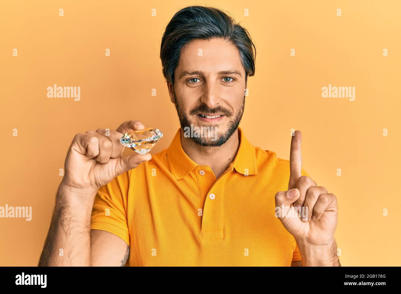 Young hispanic man holding brilliant diamond stone smiling with an idea ...