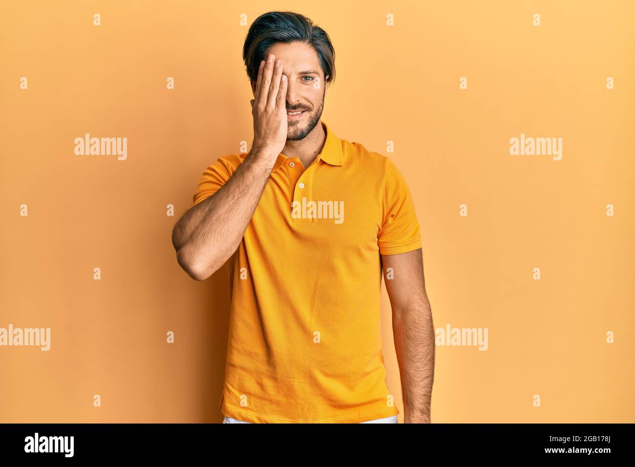Young hispanic man wearing casual yellow t shirt covering one eye with ...