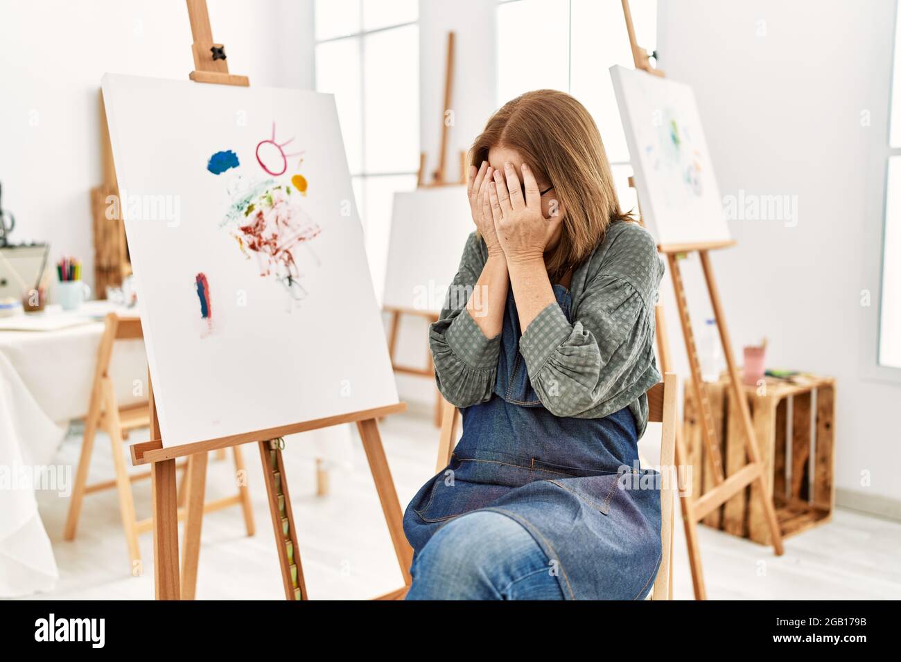 Middle age artist woman at art studio with sad expression covering face ...