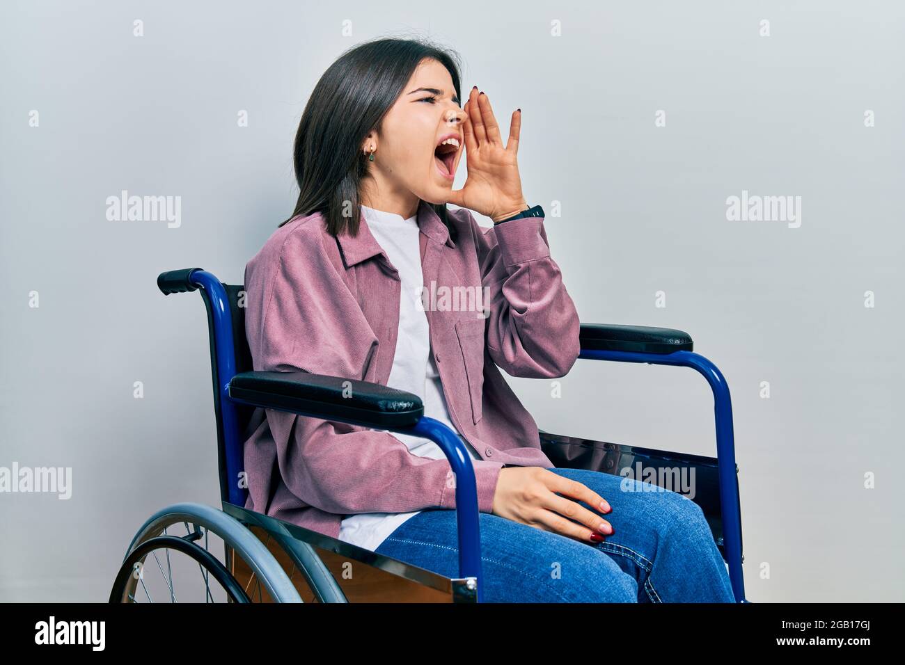 Young brunette woman sitting on wheelchair shouting and screaming loud ...