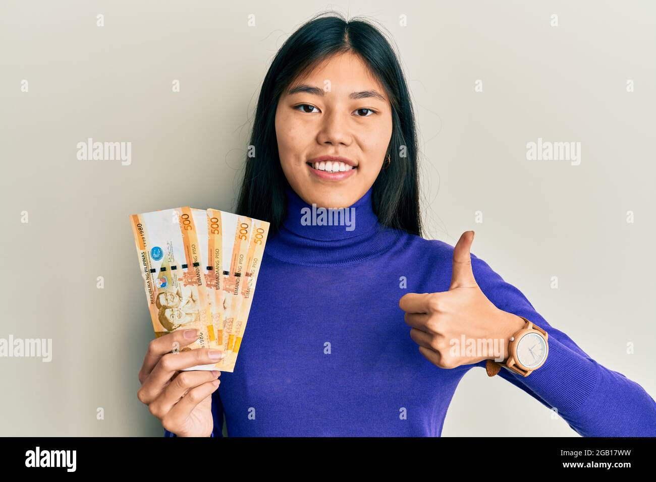 Young chinese woman holding 500 philippine peso banknotes smiling happy ...