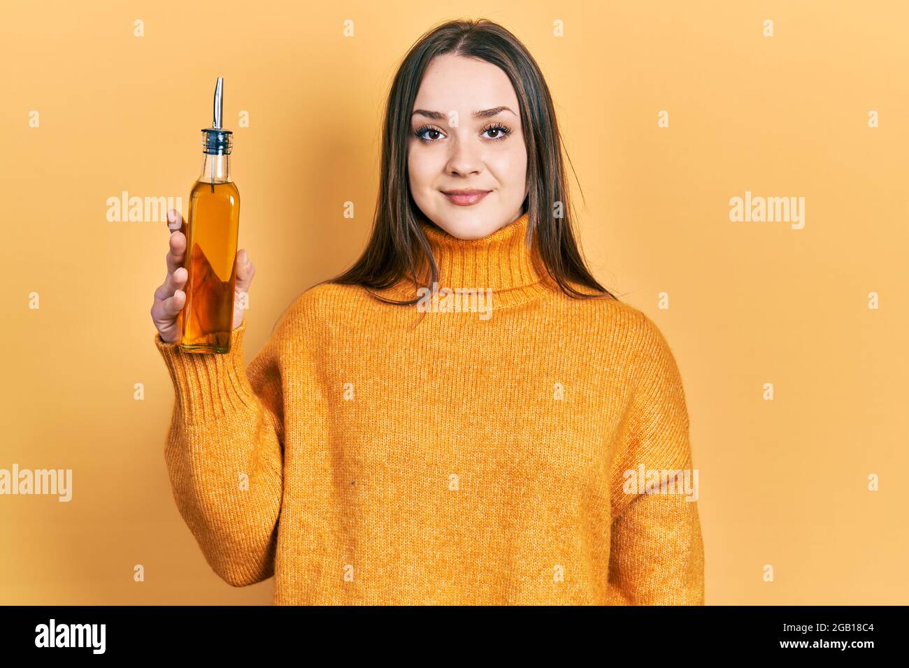 Young hispanic girl holding olive oil can looking positive and happy ...