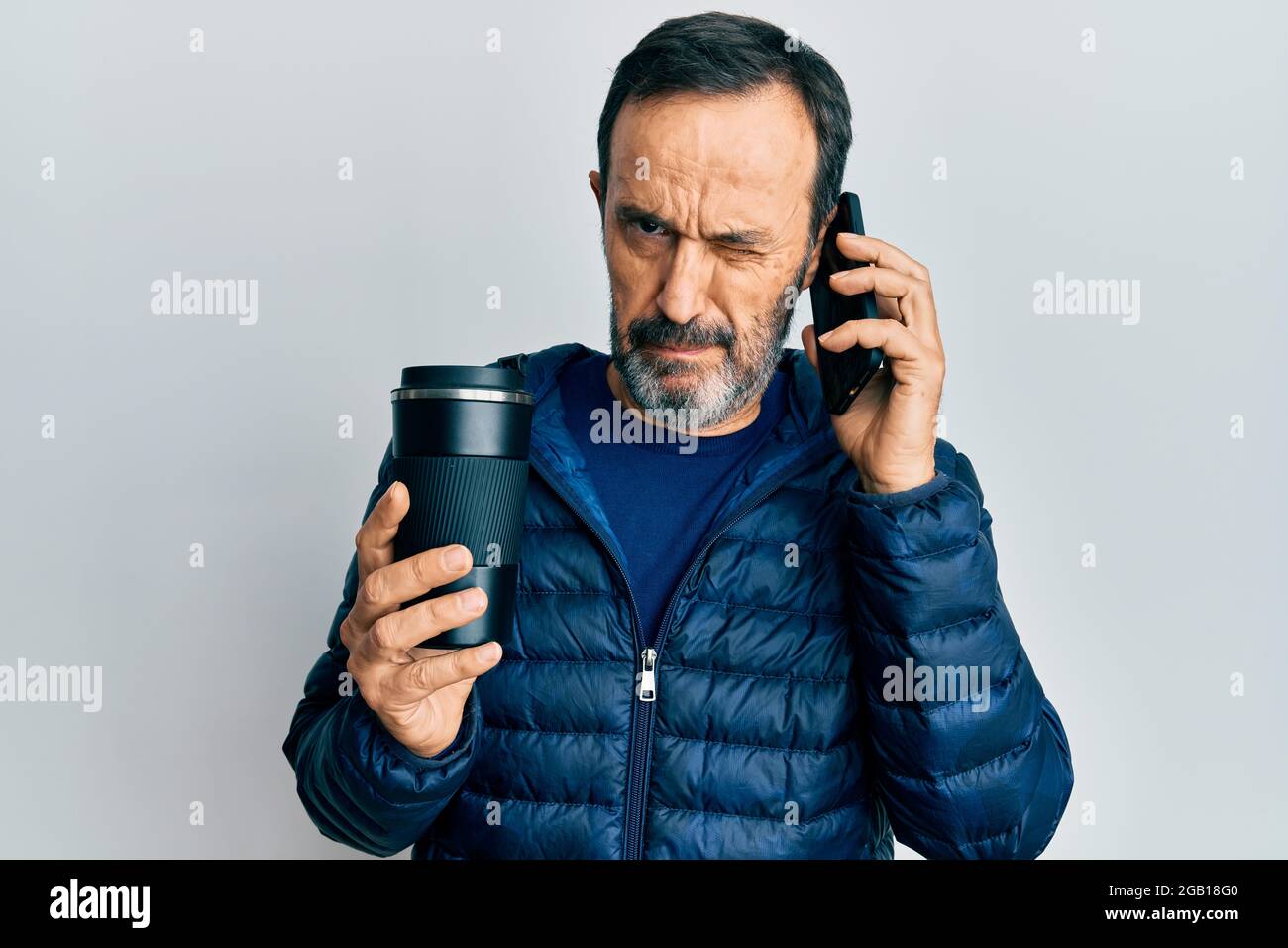 Middle age hispanic man talking on the smartphone and drinking a cup of ...