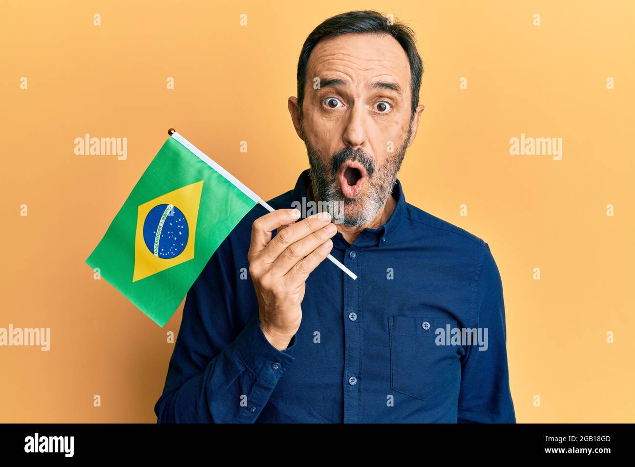 Middle age hispanic man holding brazil flag scared and amazed with open ...