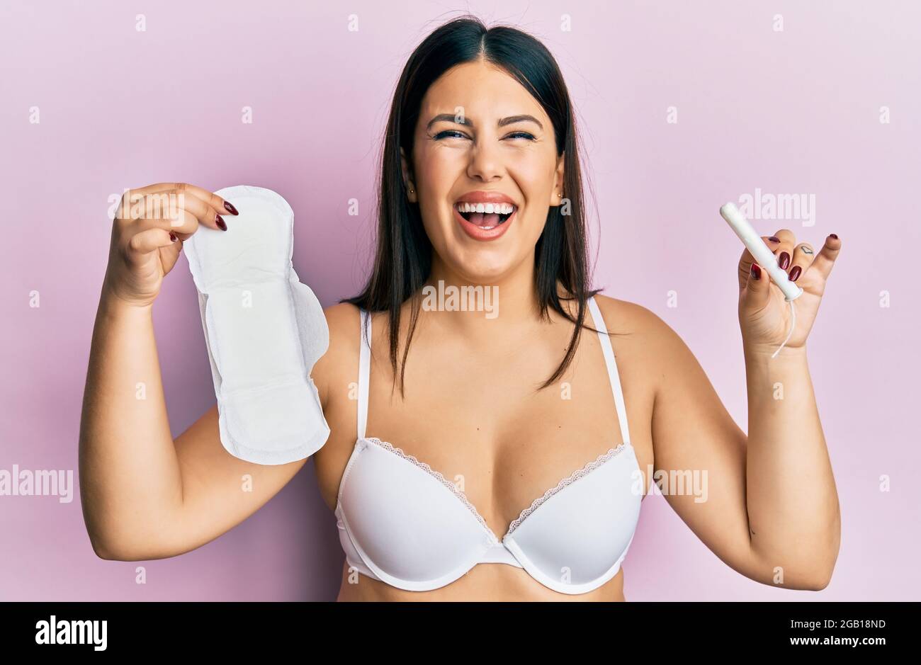 Beautiful brunette woman holding sanitary pad and cotton tampon smiling and laughing hard out ...