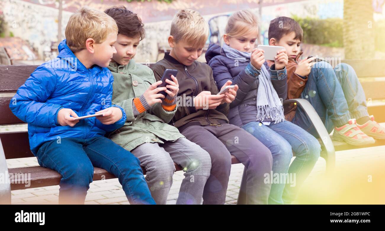 Kids playing with smartphones on bench Stock Photo - Alamy