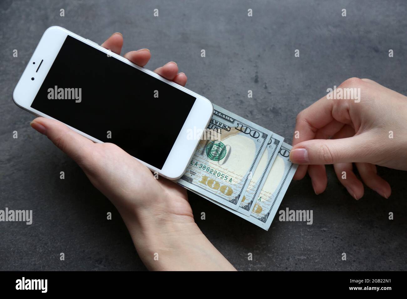 Hands holding smart phone with dollar banknotes on grey background ...