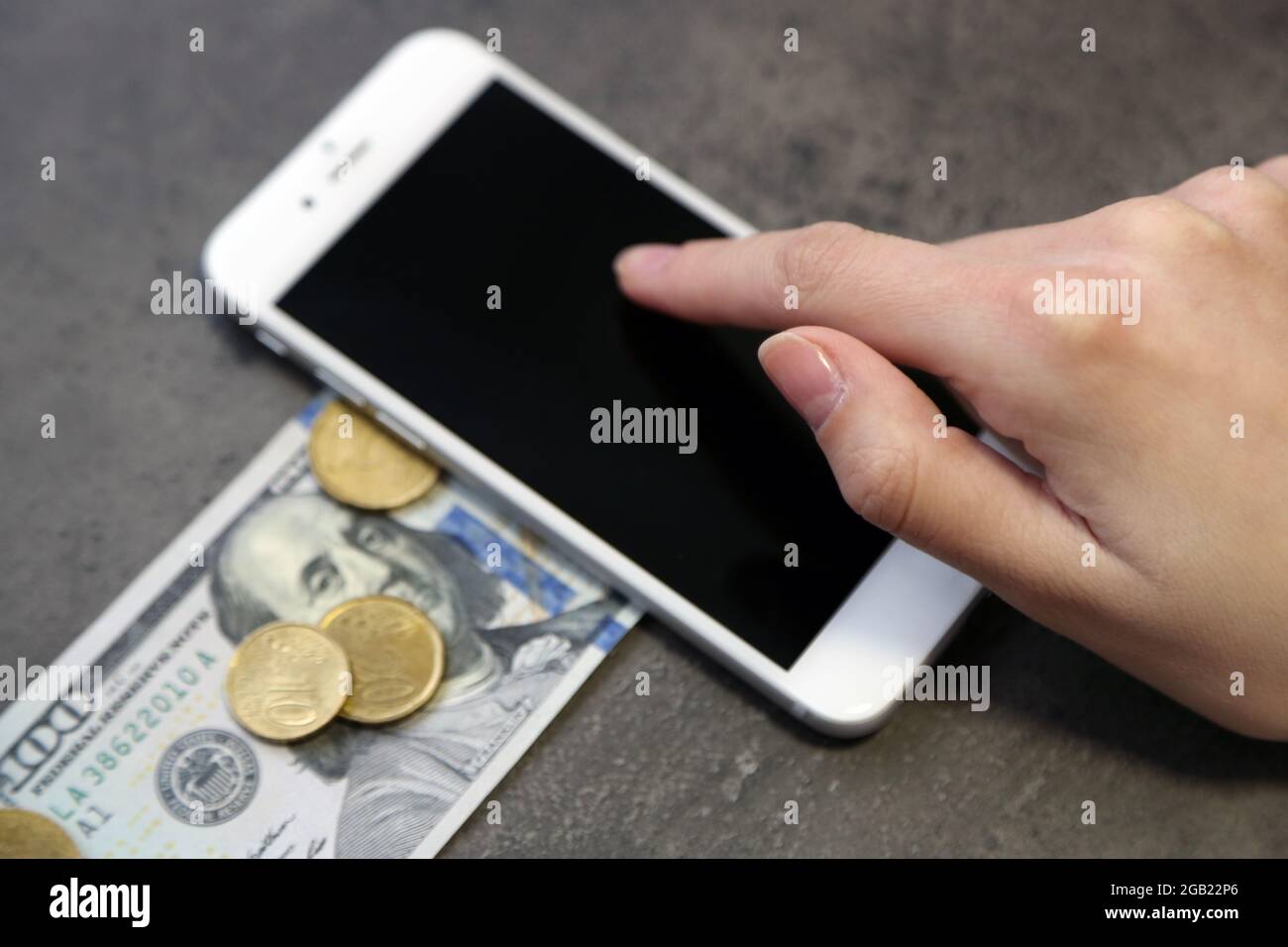 Hand with smart phone, dollar banknote and coins on grey background ...