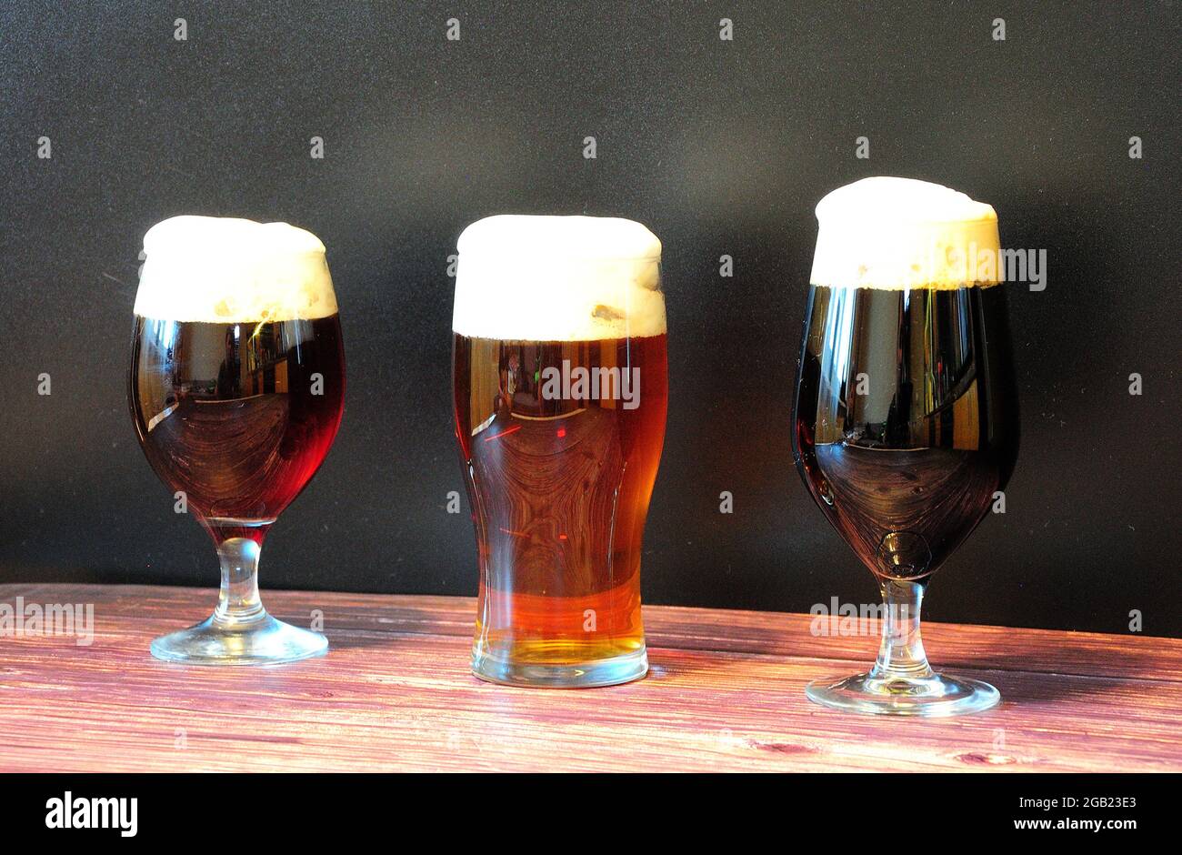 Three glasses with different types of dark beer are in a row on a ...