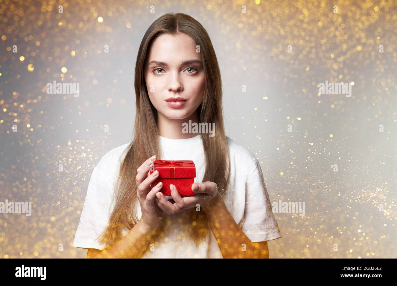 A smiling beautiful young woman holds a closed gift box with jewelry ...