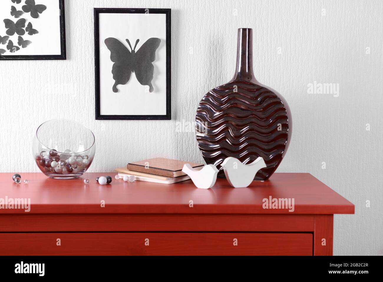 Room interior with red wooden commode, vase and frames on light wall ...