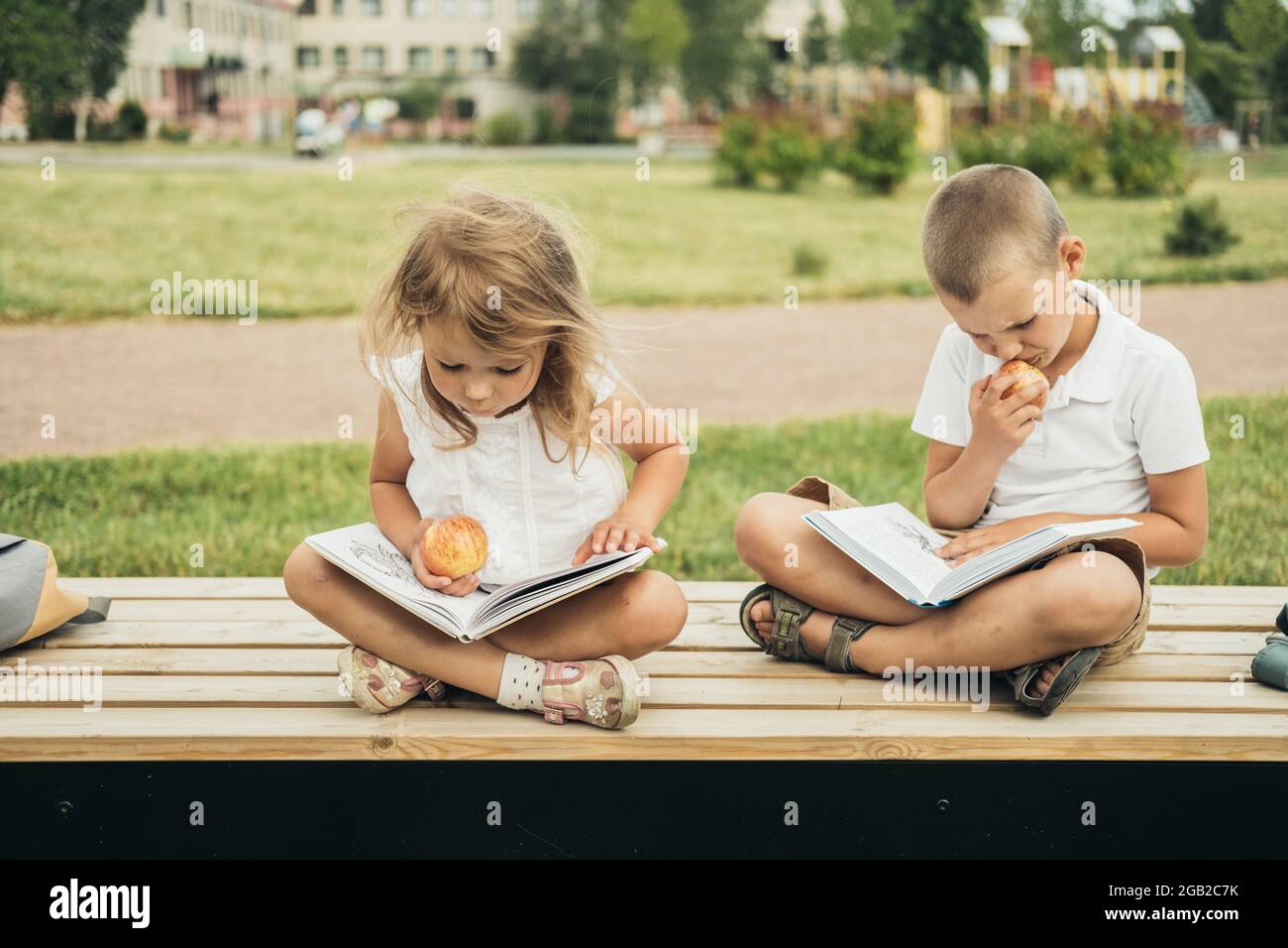 Two caucasian little students, boy and girl, eating apples during ...