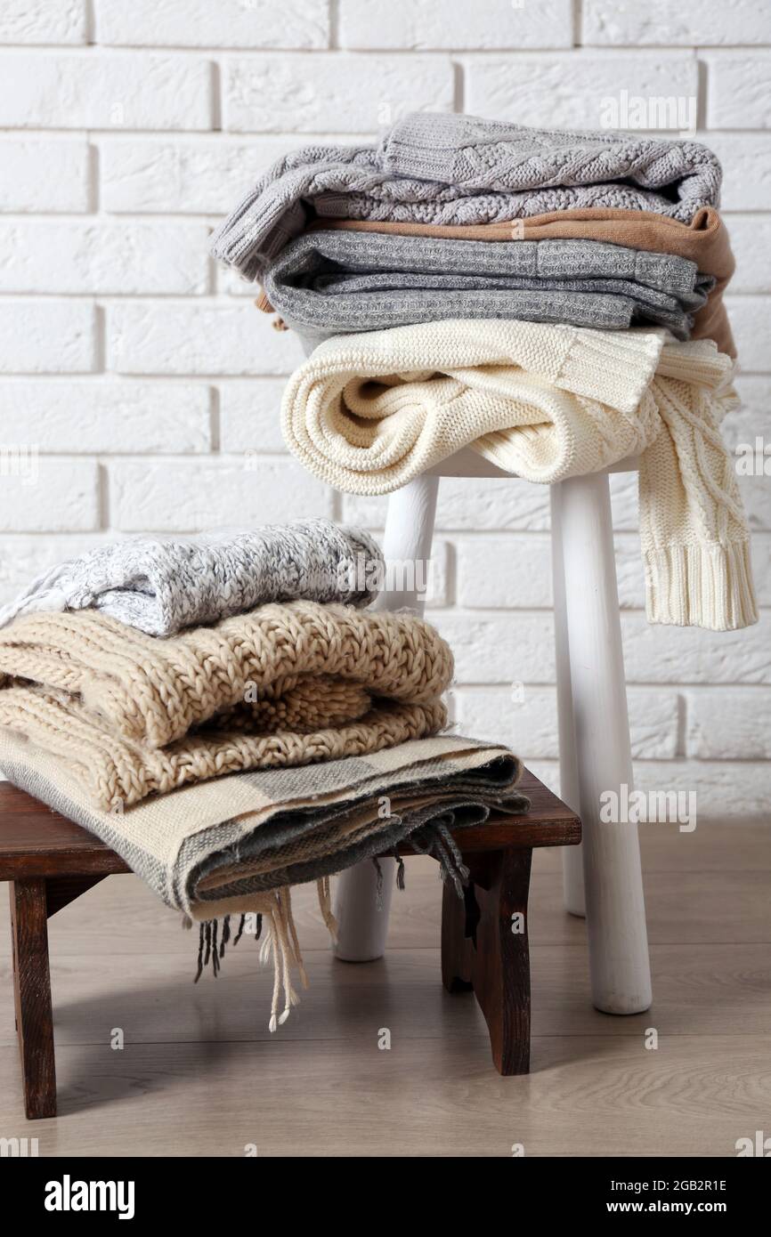 Stacks of woolen clothes on wooden stools over white brick wall ...