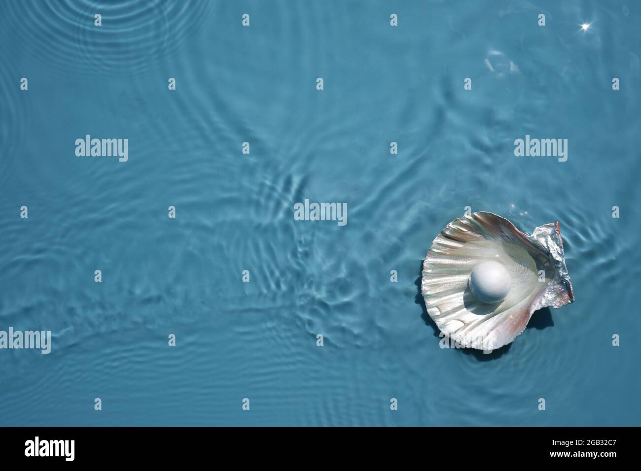Shell with a pearl on blue water Stock Photo - Alamy
