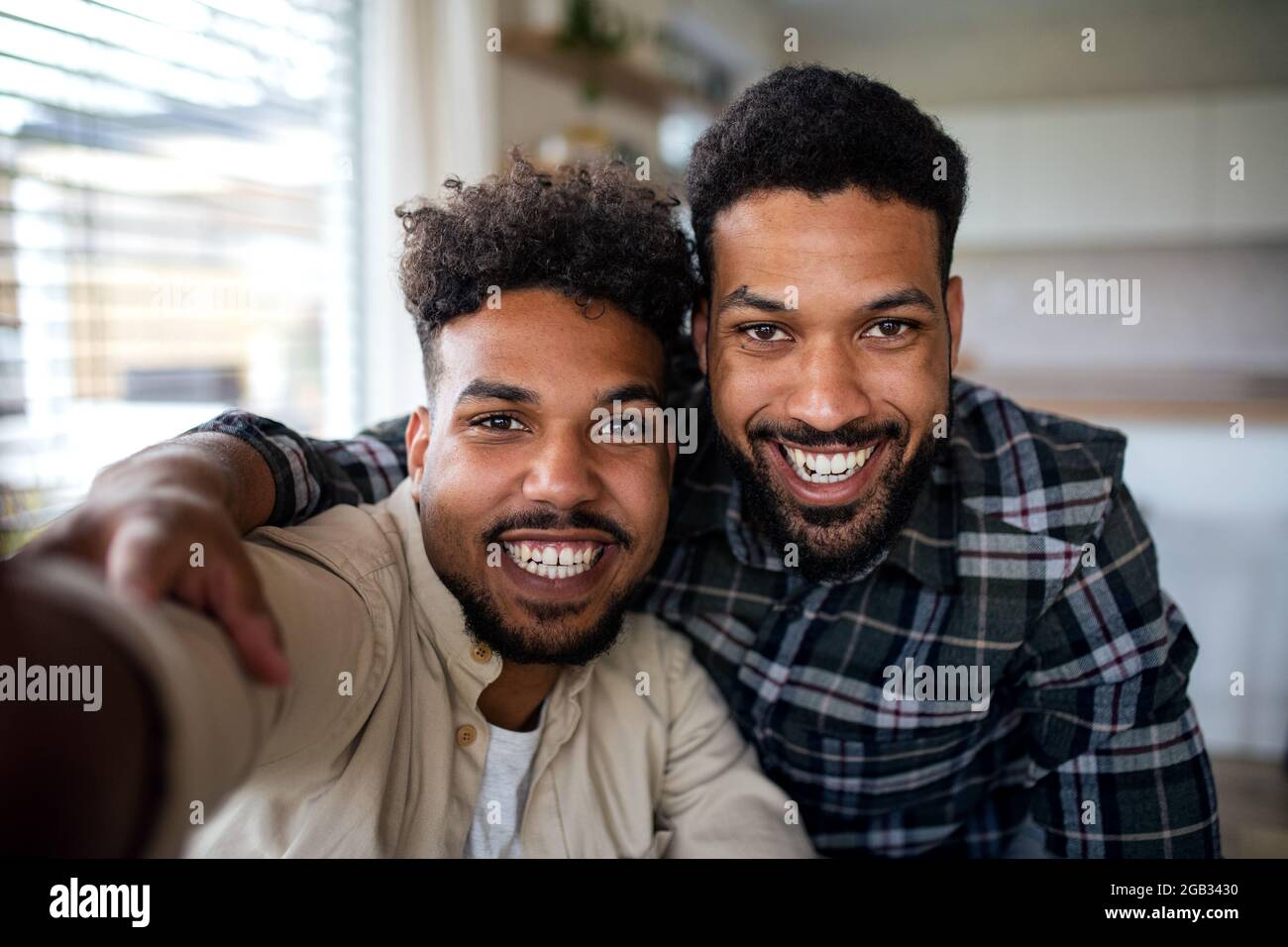 Portrait of young adult brothers in kitchen indoors at home, taking ...
