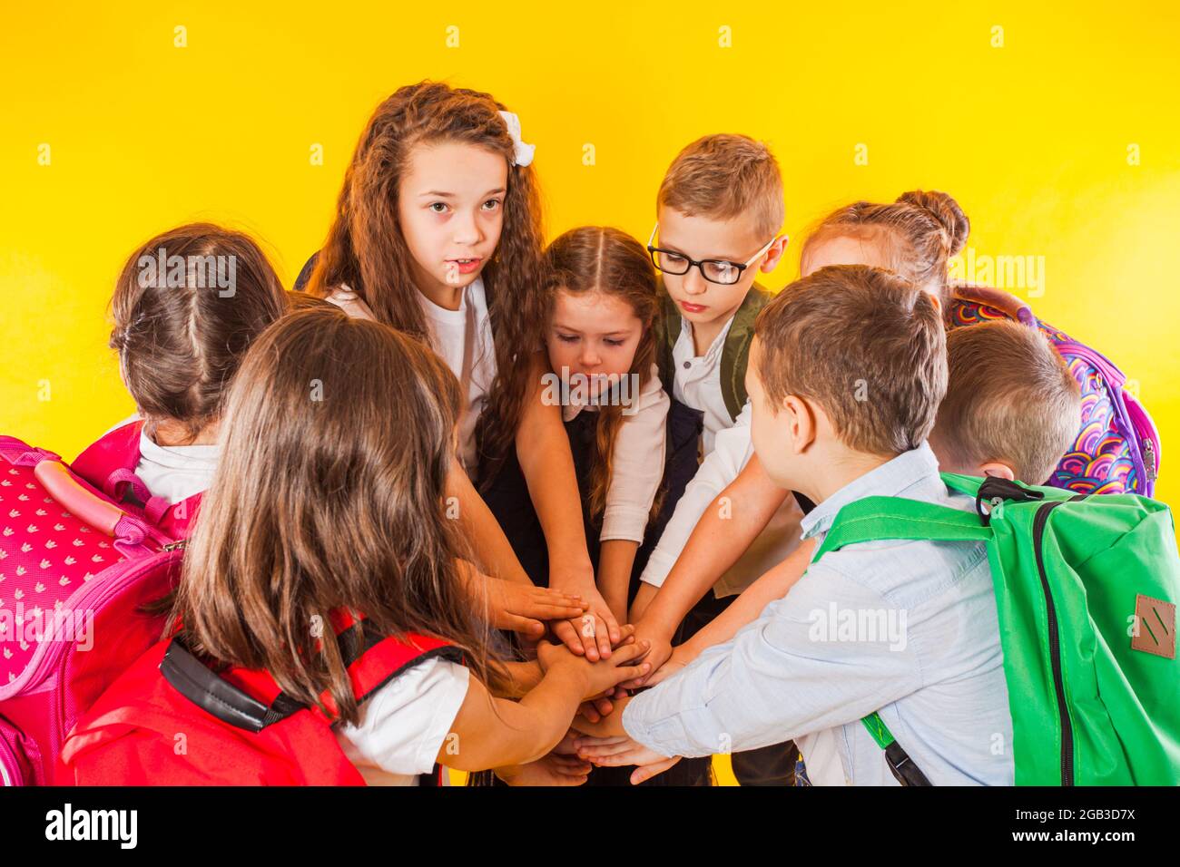 The schoolchildren are stacking hands together at the yellow background ...