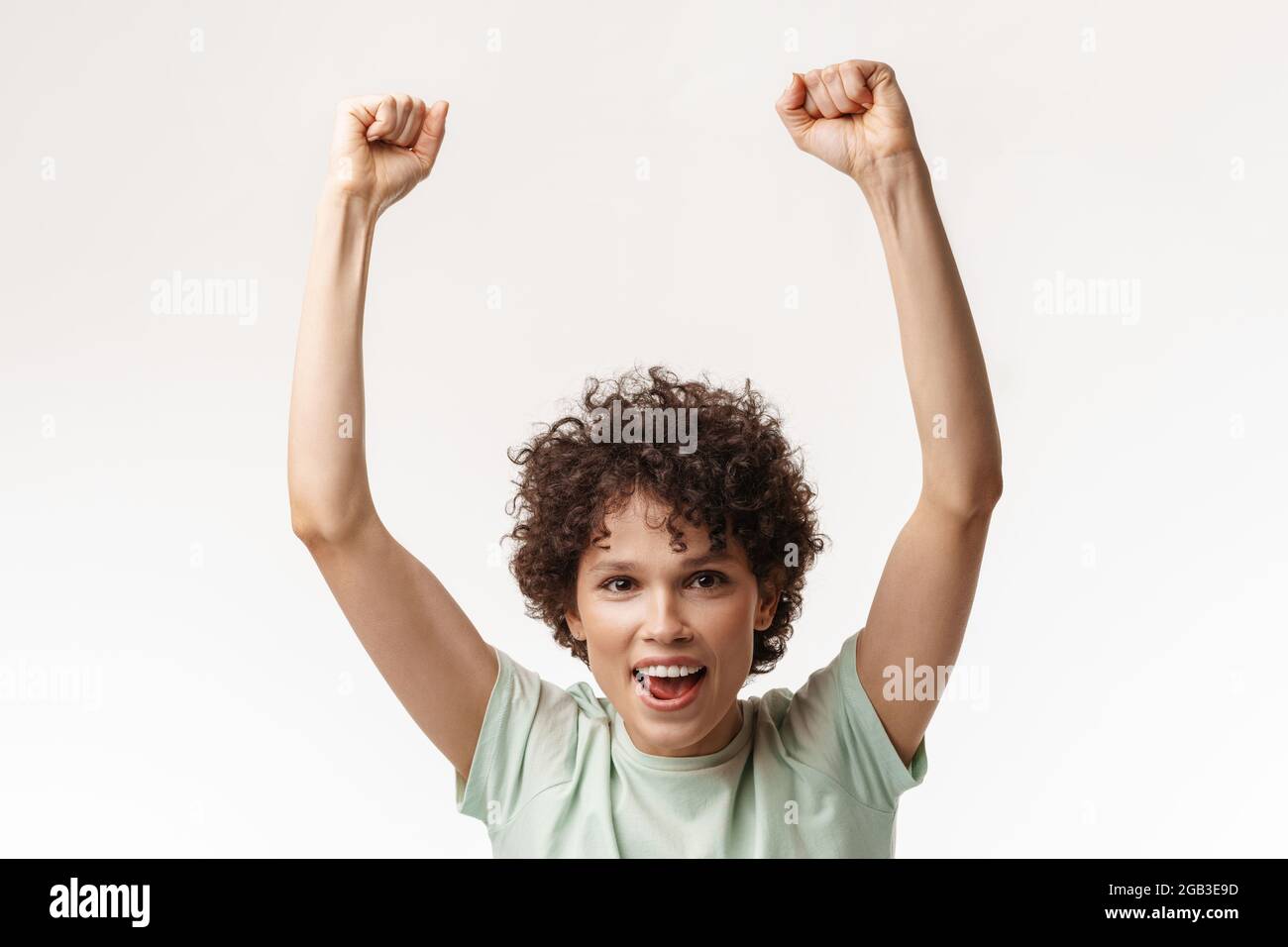 Young curly excited woman screaming while winner gesture isolated over ...