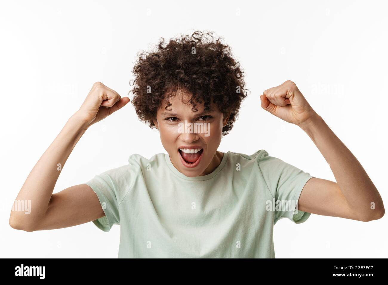 Young curly excited woman screaming while winner gesture isolated over ...