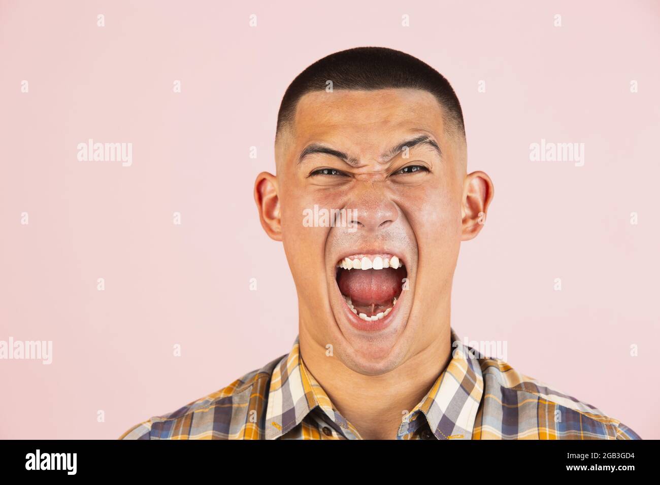 Screaming, shouting. Portrait of young handsome asian man in a plaid ...