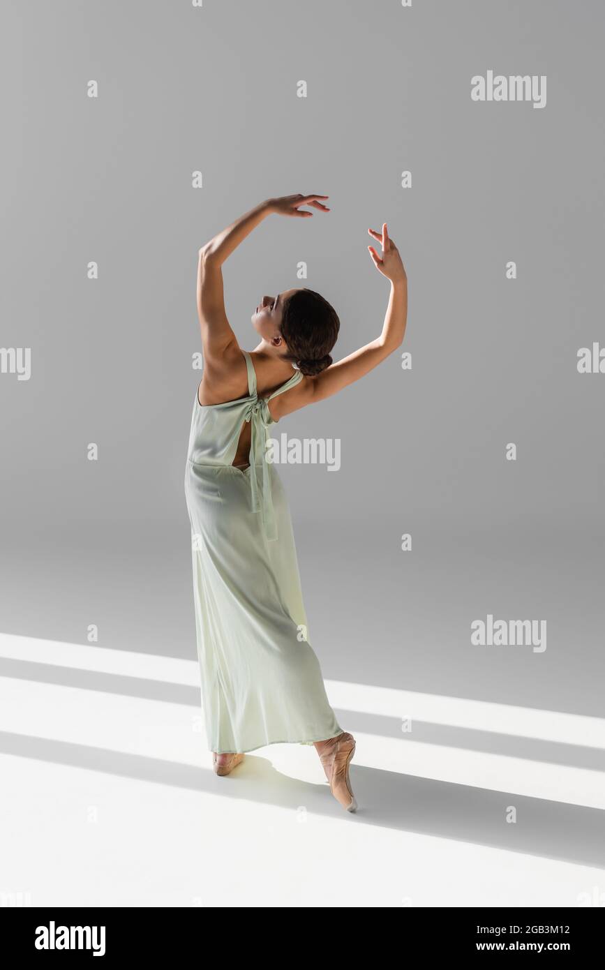 Side view of young dancer in pointe shoes standing on grey background ...