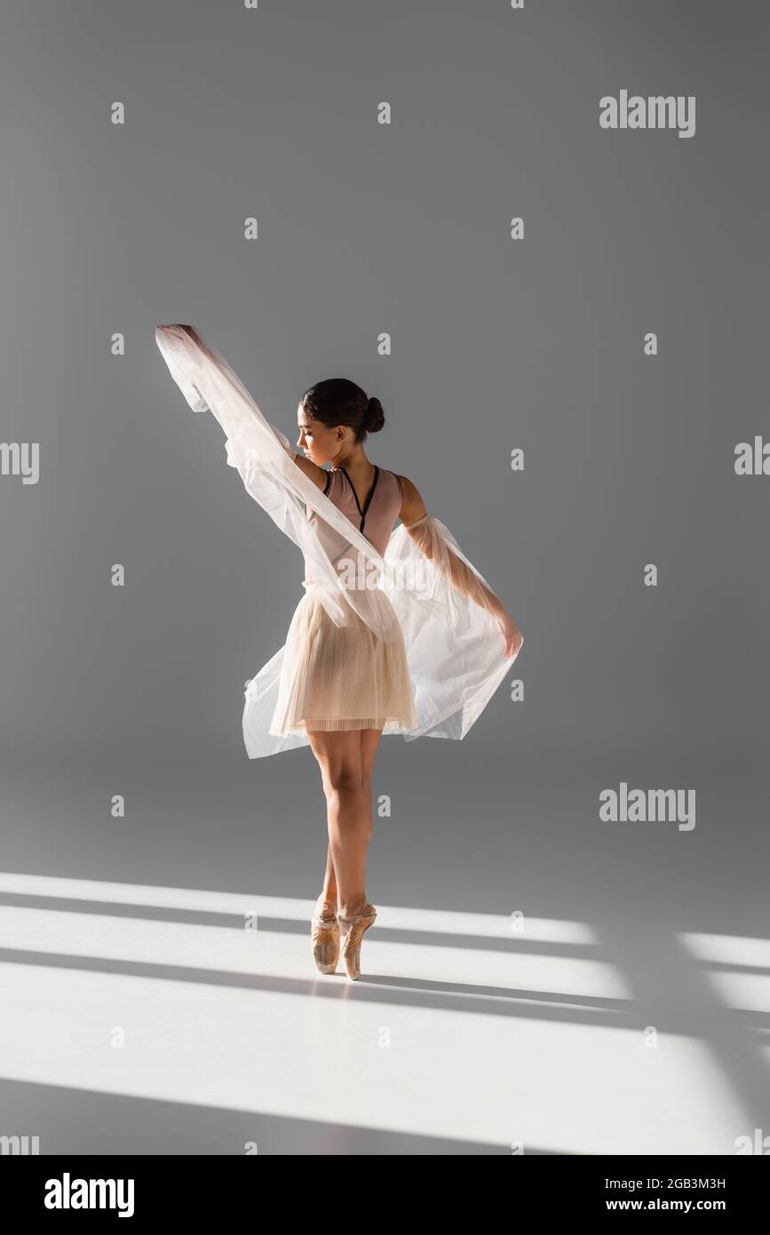 Side view of pretty ballerina dancing with white cloth on grey ...