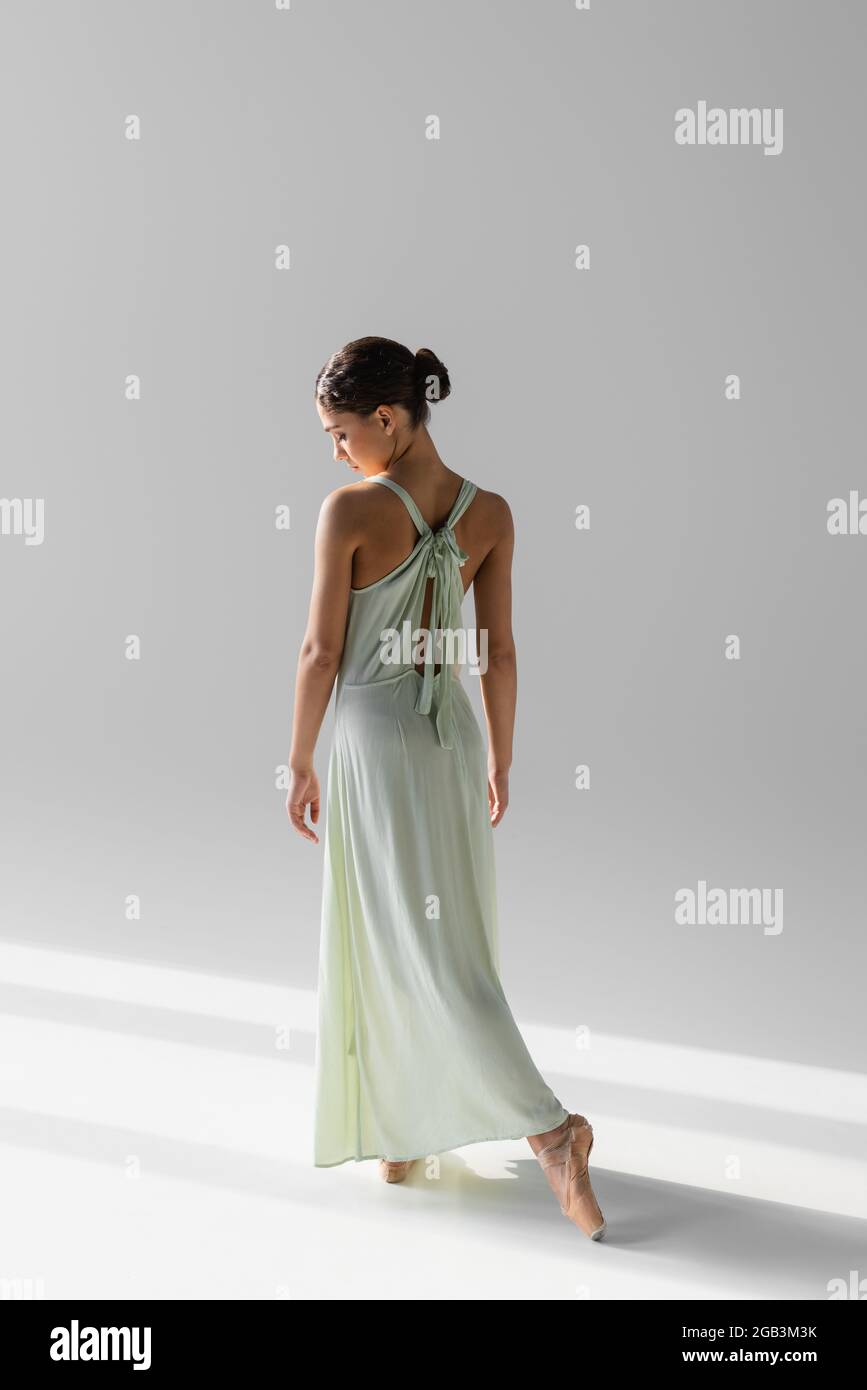 Side view of young ballerina in dress on grey background with sunlight ...