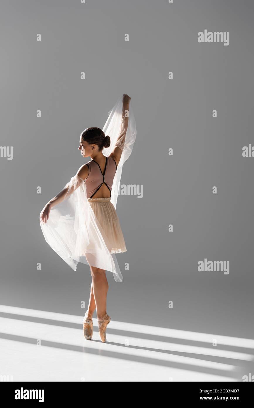 Side view of elegant ballerina dancing with white cloth on grey ...
