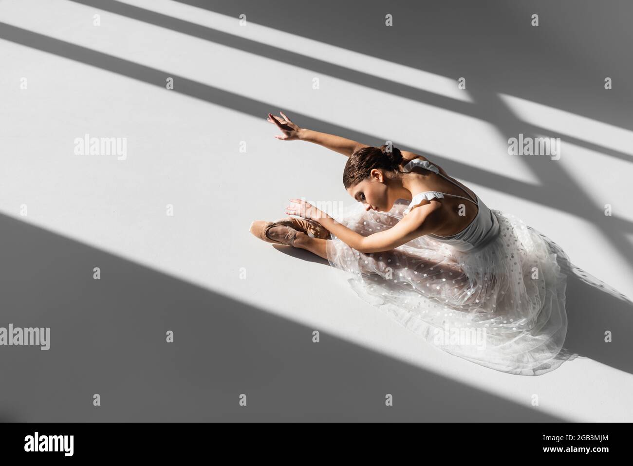 High angle view of pretty classical dancer bending on floor on grey ...