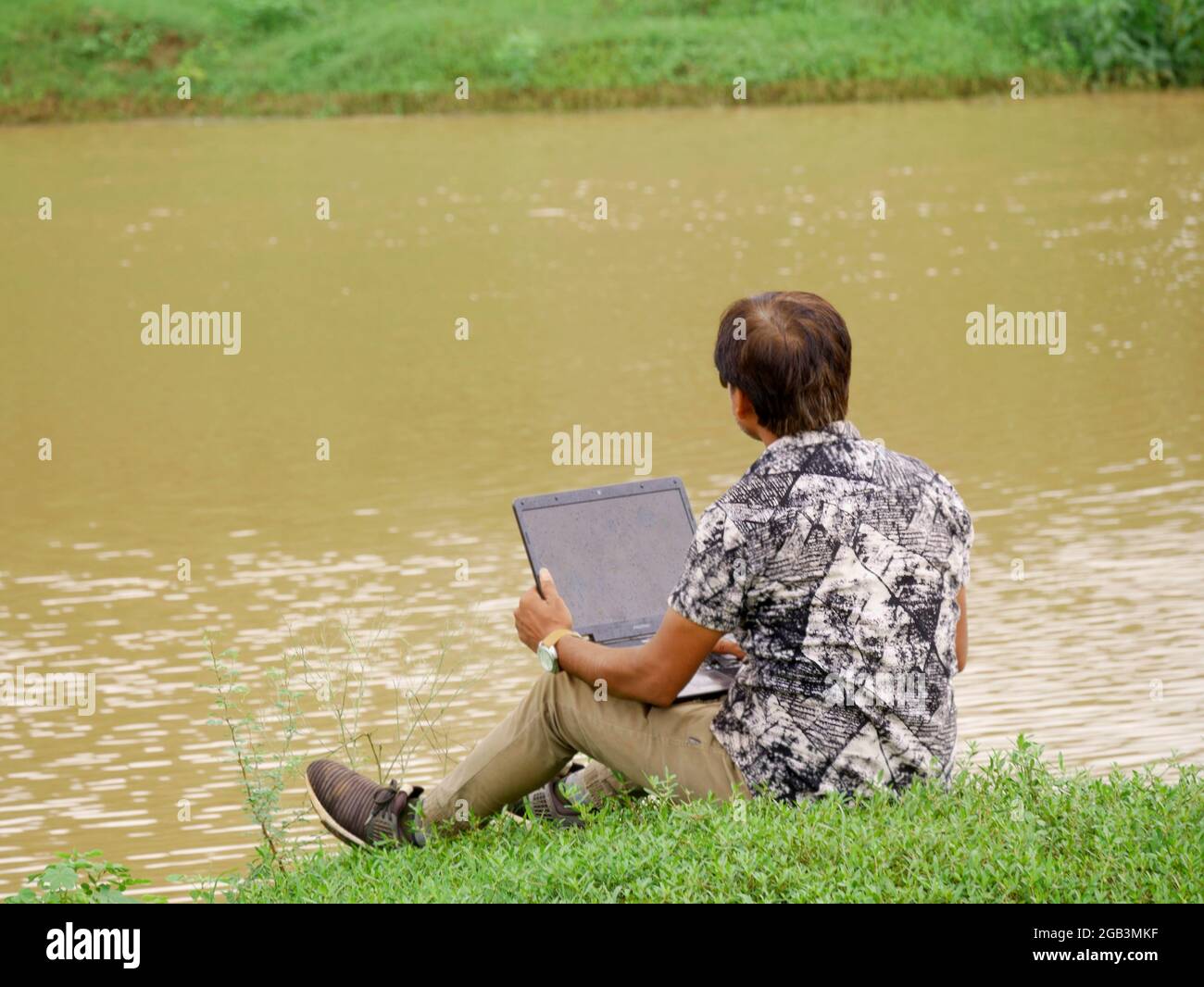 Indian city boy operating laptop at river bank during raining season ...