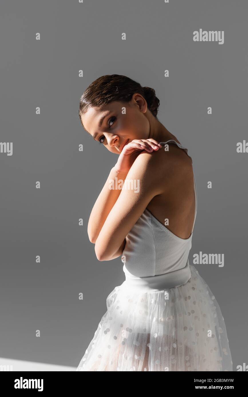 Pretty ballerina looking at camera on grey background with sunlight ...