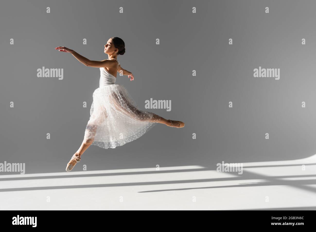 Side view of professional ballerina jumping on grey background with ...