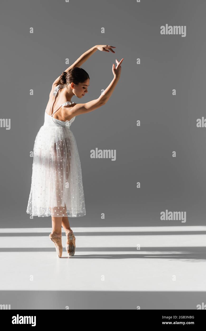 Side view of ballerina bending and looking down on grey background with ...