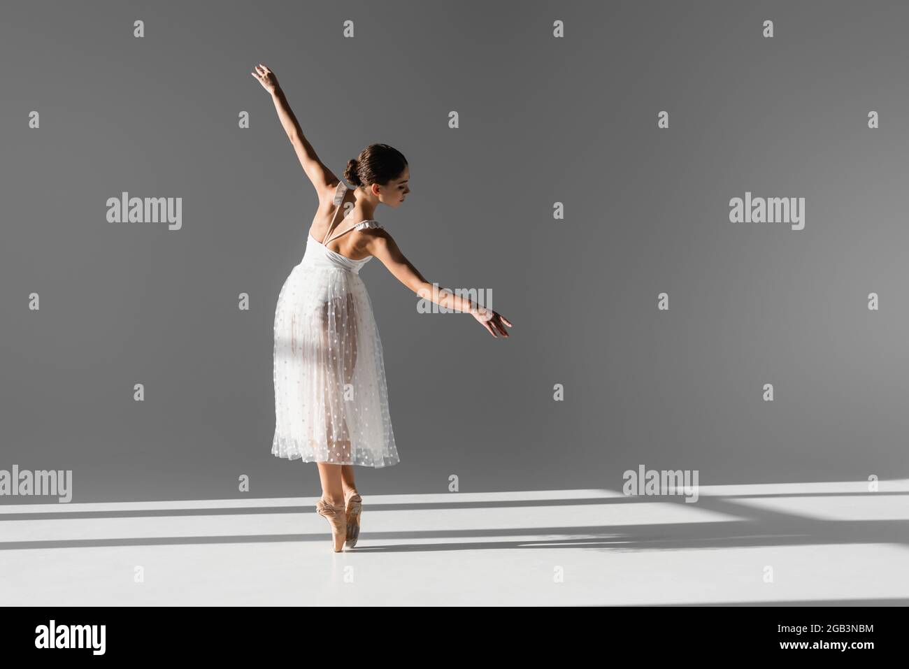 Side view of elegant ballerina in pointe shoes on grey background with ...
