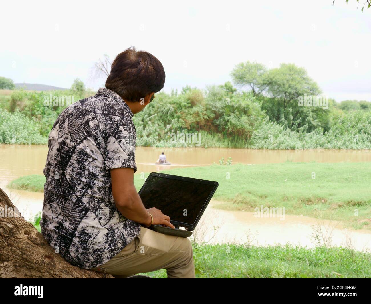 Indian city man operating laptop computer at river bank, natural ...