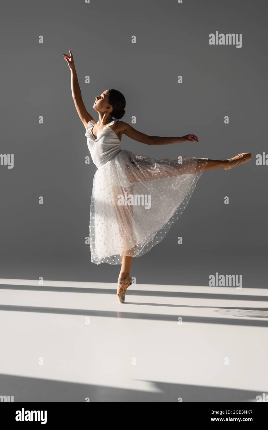 Side view of elegant ballerina dancing on grey background with sunlight ...