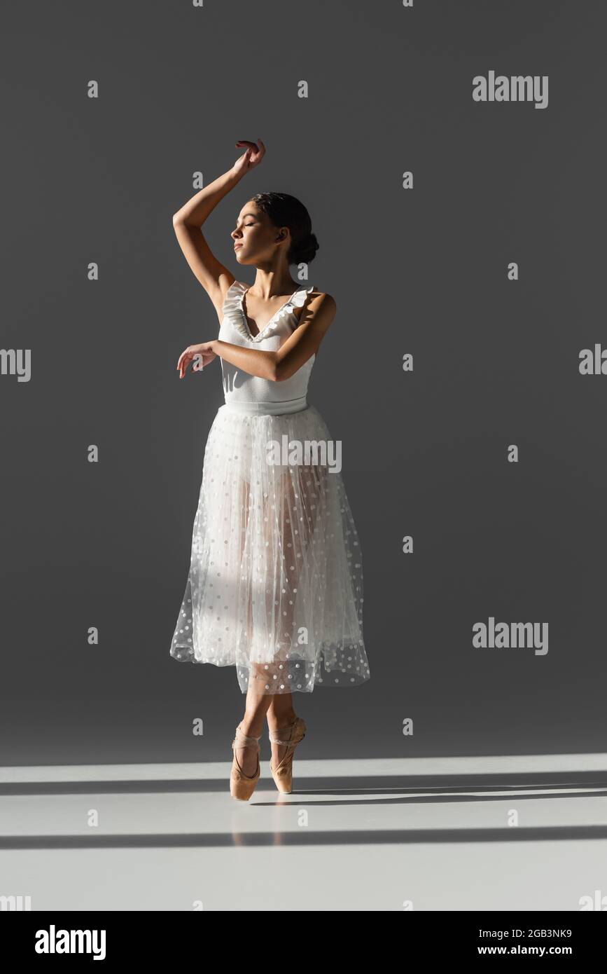 Side view of young ballerina with closed eyes dancing on grey ...