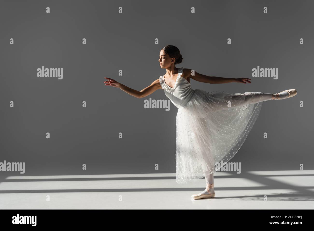 Side view of ballerina in white skirt dancing on grey background with ...