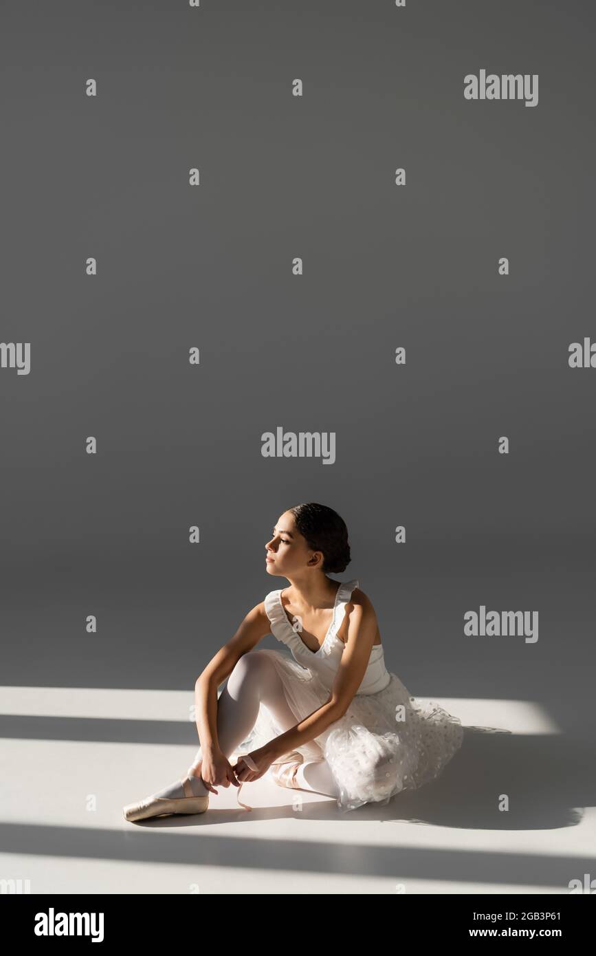 Side view of ballerina in dress sitting on grey background Stock Photo ...