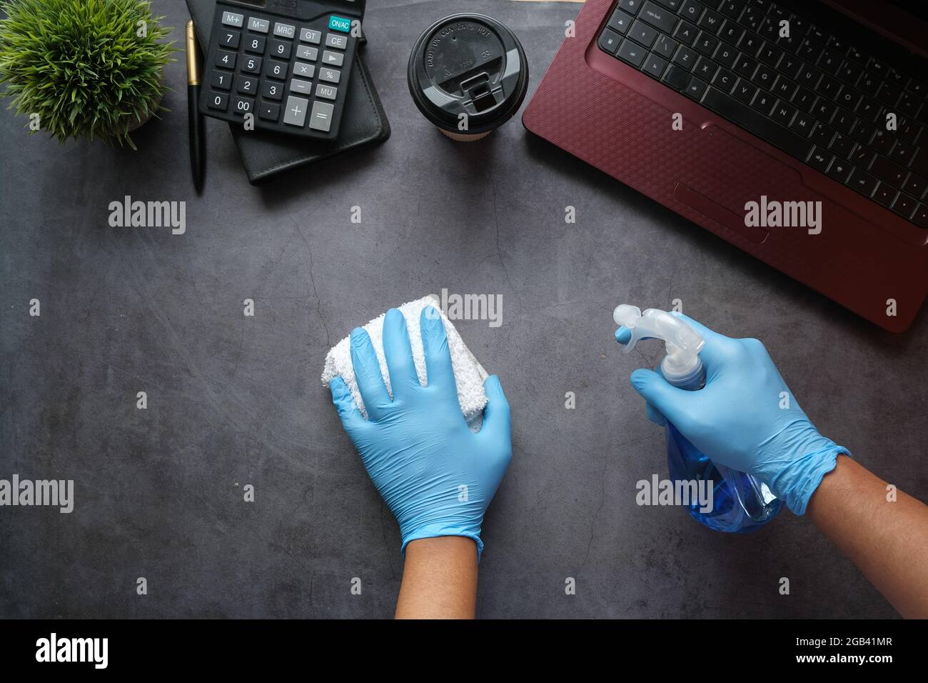 hand in blue rubber gloves holding spray bottle cleaning office table ...