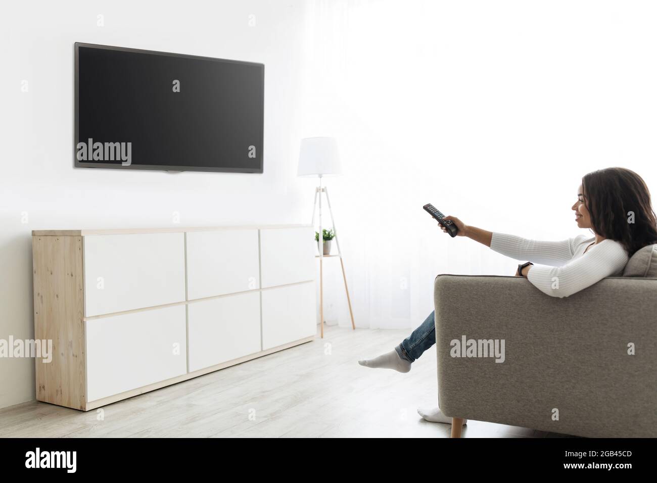 Lady watching TV holding remote control and switching channels on ...