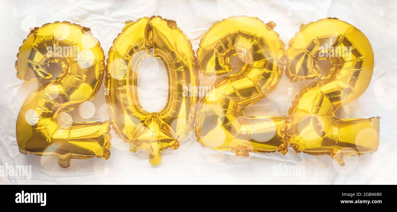 2022 new year numbers in golden foil balloons on white sheet background with festive lights ...