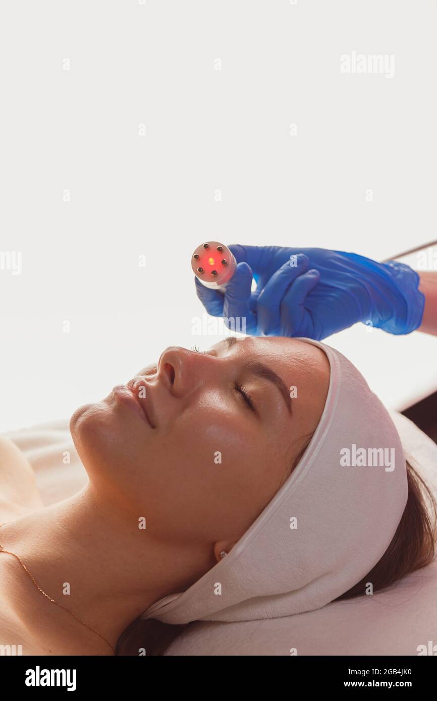 Young woman getting microcurrents skin cleansing and face treatment at beauty salon. Beautician ...