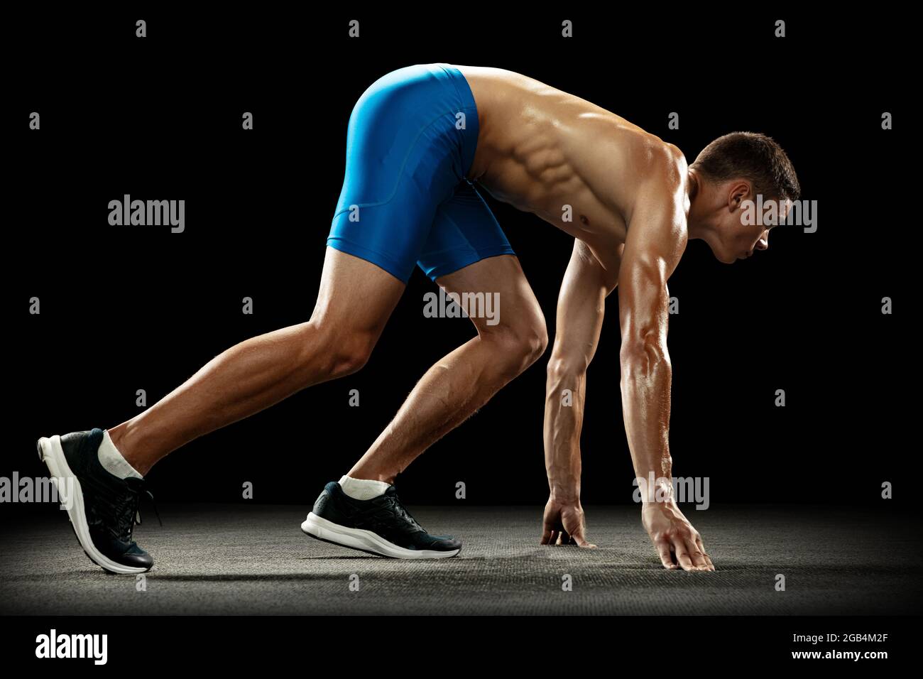 Side view of young professional male athlete, runner preparing to start ...