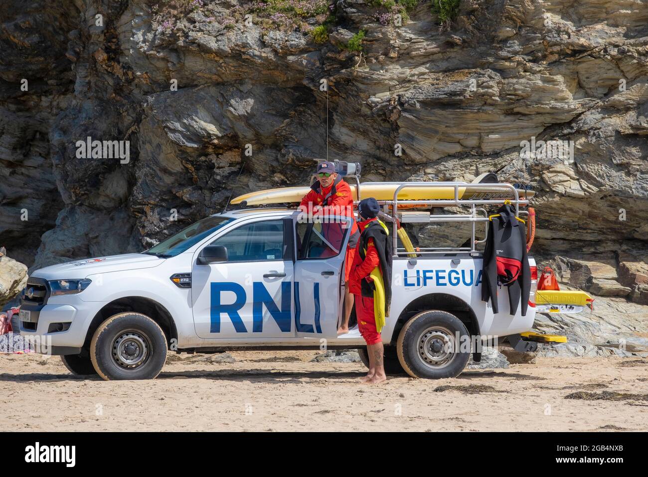 Two RNLI Lifeguards chatting on Mawgan Porth Beach in Cornwall with an ...