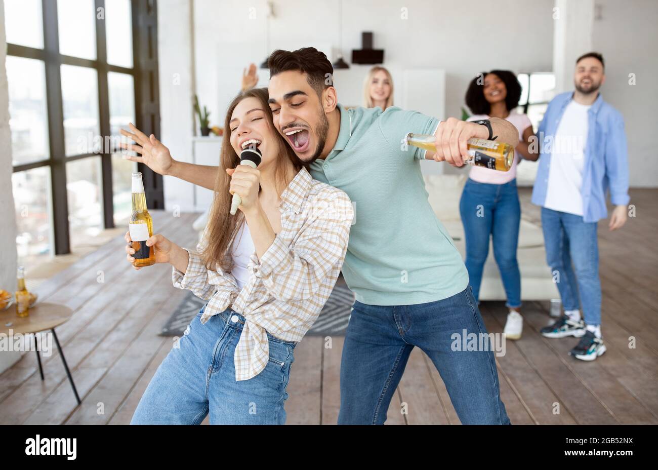 Millennial multiethnic couple singing song into microphone, drinking ...